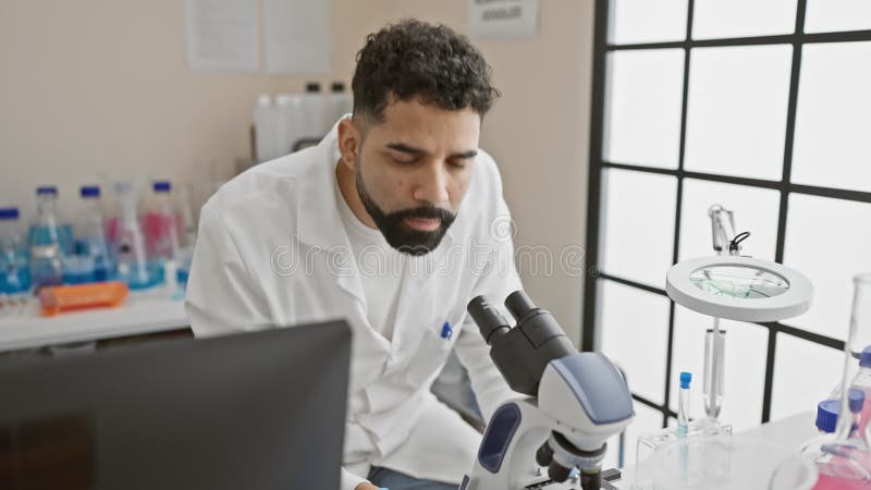 A Focused Hispanic Man with a Beard Wearing a Lab Coat Examines a ...