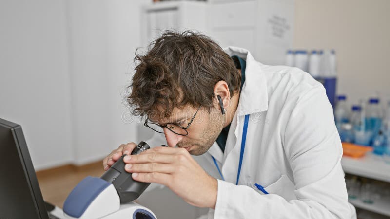 A Focused Hispanic Man with a Beard and Wireless Earbuds Examines ...