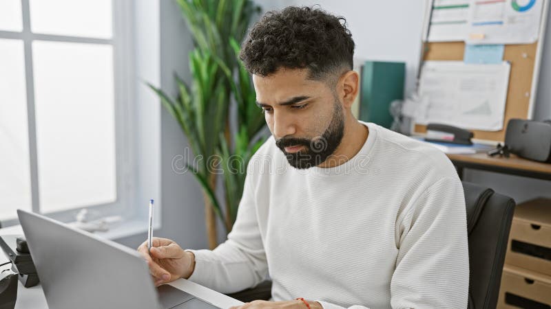 A Focused Hispanic Man with a Beard Working in an Office, Using a ...