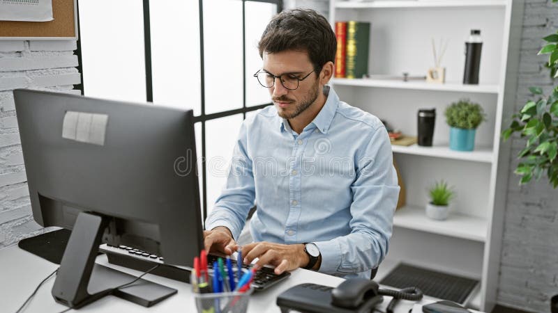 A Focused Hispanic Man with a Beard Works at a Computer in a Modern ...