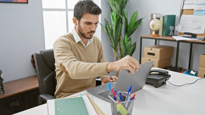 Focused Hispanic Man With Beard Works On Laptop In A Modern Organized