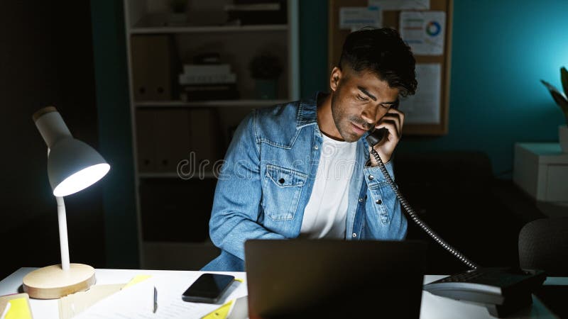 A Focused Hispanic Man in a Denim Jacket Speaking on the Phone at Night ...