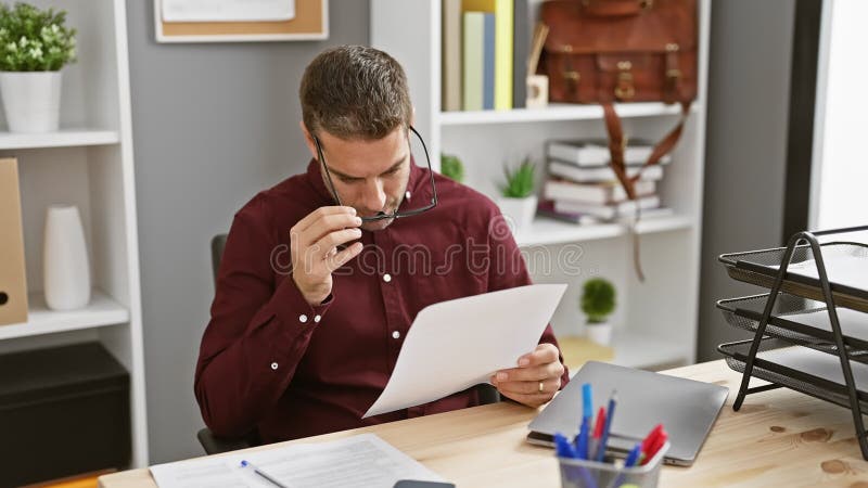Focused Hispanic Man with Glasses Examining a Document in a Modern ...