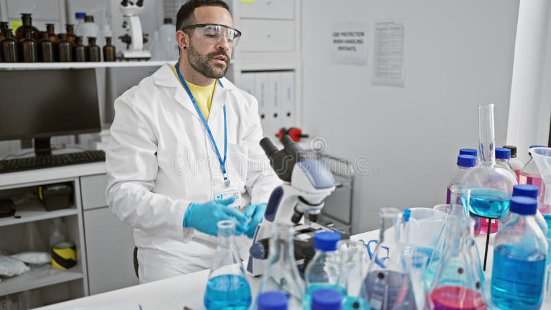 A Focused Hispanic Man in Lab Coat Using Microscope in Laboratory ...
