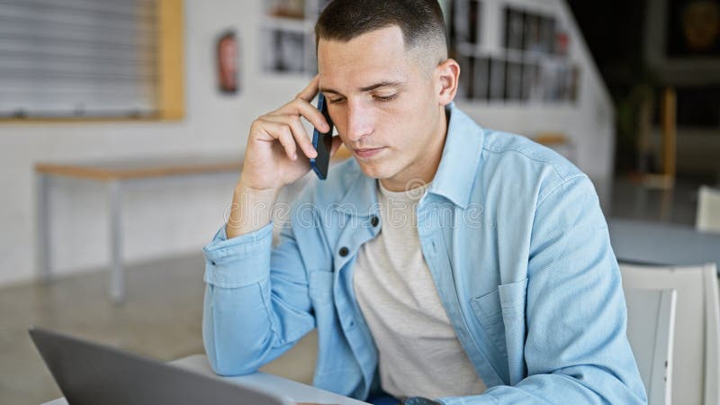 A Focused Hispanic Man Talks on a Smartphone while Working on a Laptop ...