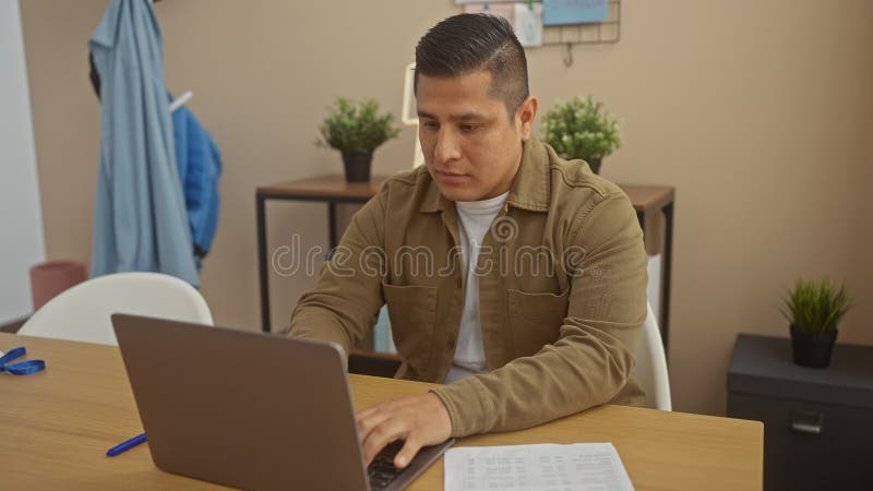 Focused Hispanic Man Using Laptop in a Modern Home Interior Setting ...