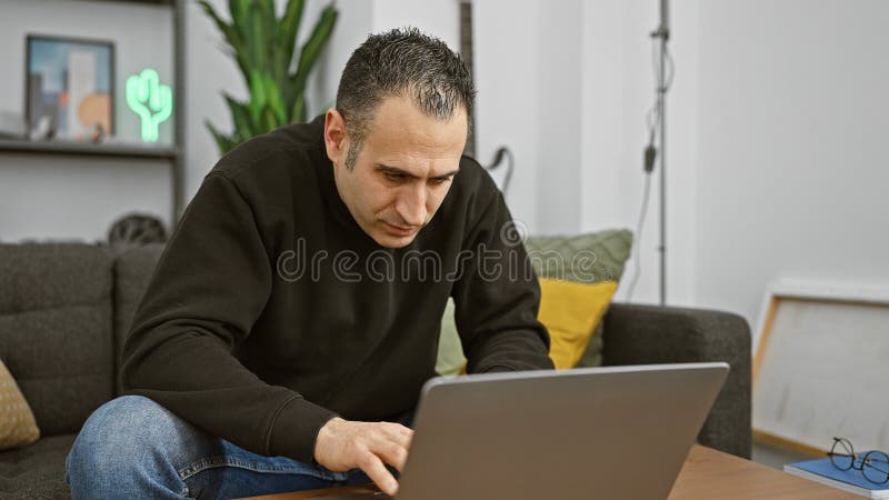 Focused Hispanic Man Using Laptop in a Modern Living Room Setting Stock ...