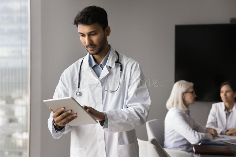 Focused Indian General Practitioner Wears White Coat Use Digital Tablet ...