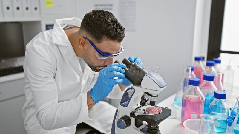 A Focused Male Scientist Examines a Specimen with a Microscope in a ...