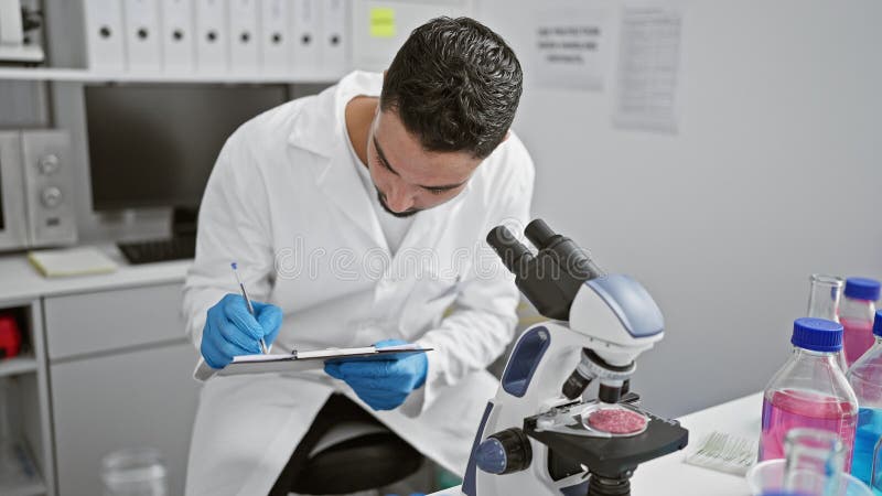 A Focused Man in a Lab Coat Examines a Slide Under a Microscope in a ...