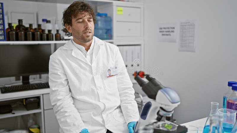 A Focused Man in a Lab Coat Examining Specimens Under a Microscope in a ...