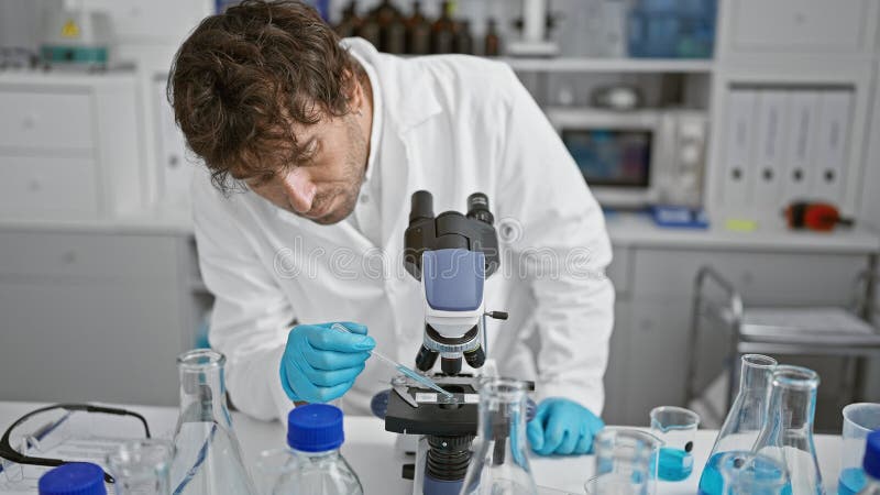 A Focused Man in Lab Coat Uses Microscope in a Well-equipped Laboratory ...