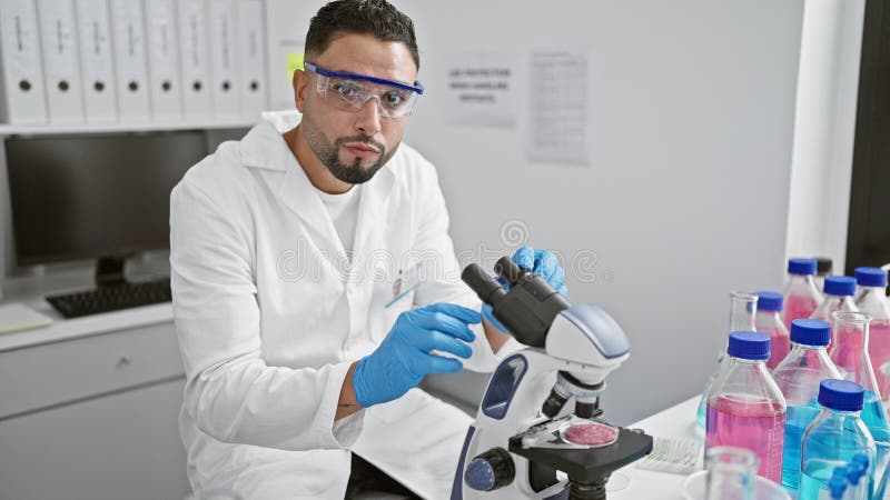 A Focused Man in a Lab Coat Using a Microscope in a Modern Laboratory ...