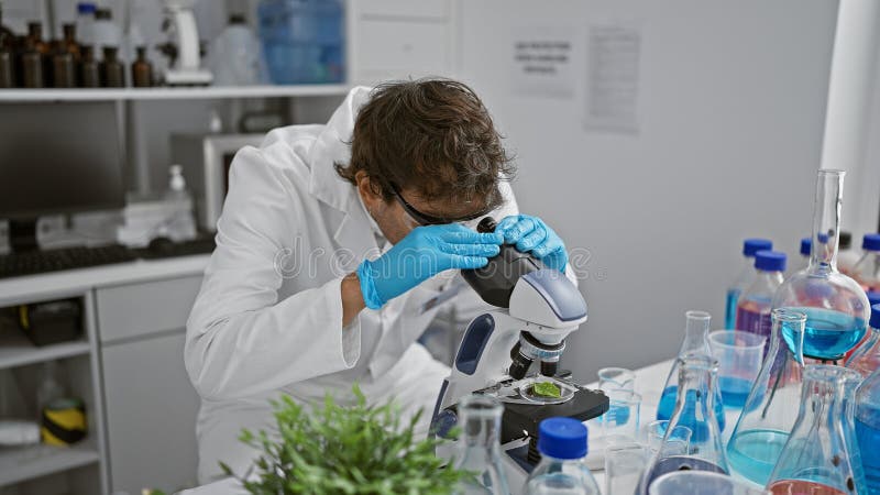 A Focused Man Studies Samples Using a Microscope in a Modern Laboratory ...