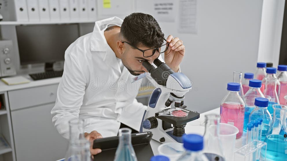 A Focused Man Using a Microscope in a Laboratory Setting, Surrounded by ...