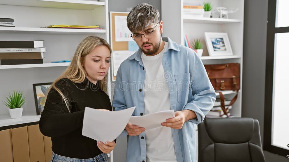A Focused Man and Woman Evaluate Documents Together in a Modern Office Setting, Showcasing ...