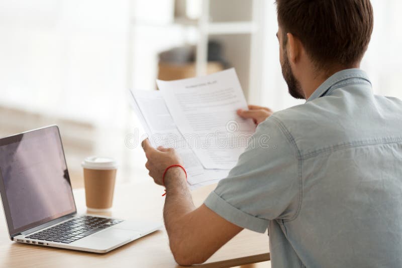 Focused Man Working at Laptop Reading Paperwork Documents Stock Image ...