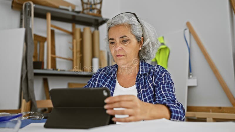 A Focused Mature Woman Carpenter Using Tablet in a Well-lit Workshop ...
