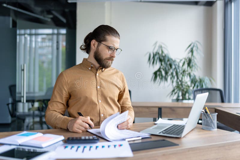 Professional Man Reviewing Reports at Desk with Laptop in Modern Office ...