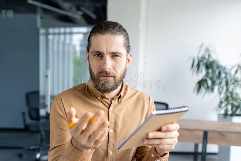 Serious Man in an Office Setting Holding a Notepad and Asking Questions ...