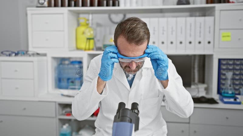 A Focused Scientist Adjusts Safety Goggles before Using a Microscope in ...
