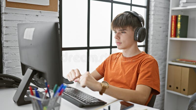 A Focused Teenage Boy Wearing Headphones Studies at a Computer in a ...