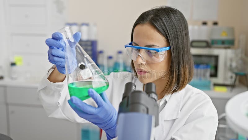 A Focused Woman Scientist Conducts an Experiment with a Green Liquid in ...