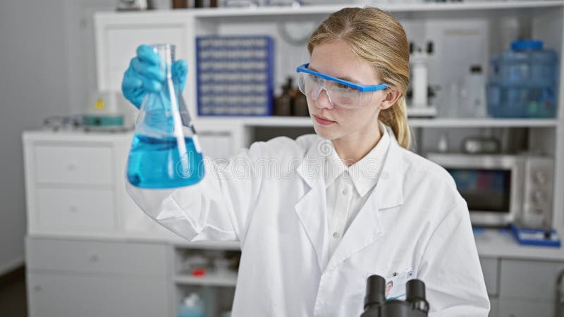 A Focused Woman Scientist Examining a Blue Liquid in a Flask in a ...