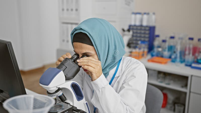 A Focused Woman Scientist Using a Microscope in a Modern Laboratory ...