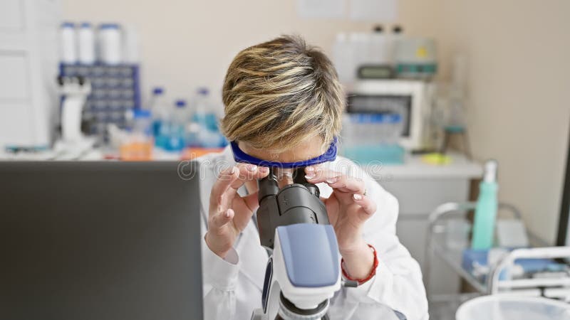A Focused Woman Scientist Using a Microscope in a Modern Laboratory ...
