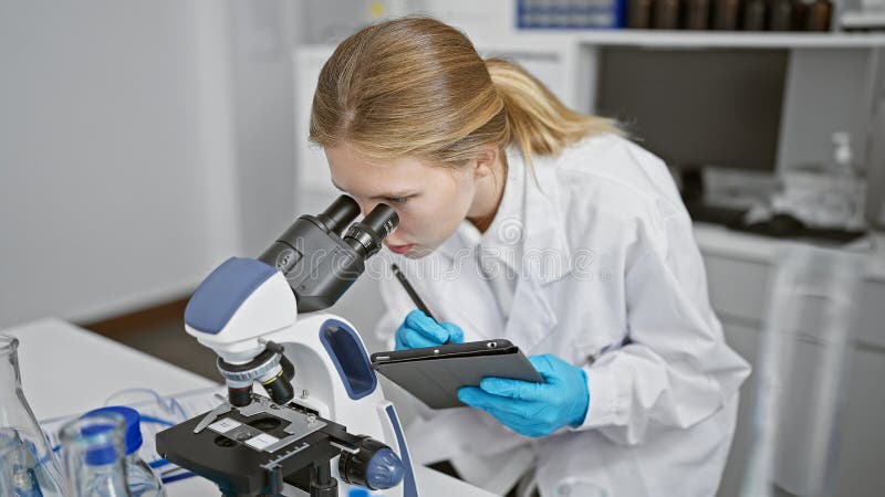 Focused Woman Scientist Using Microscope and Taking Notes in a ...