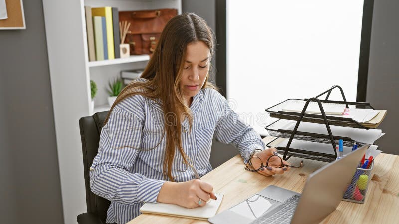 Focused Woman Writing Notes in a Modern Office Setting, with Laptop and ...