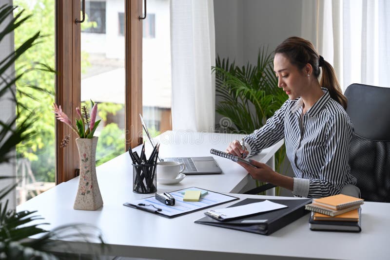 Focused Working Woman Using Laptop and Writing Ideas in a Notebook ...