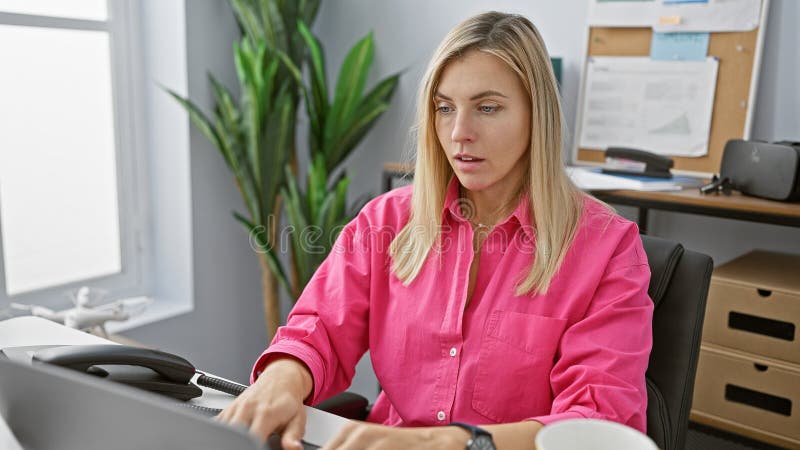 Focused Young Blonde Woman Working Diligently at Her Desk in a Bright ... Focused Young Blonde Woman Working Diligently at Her Desk in a Bright ...