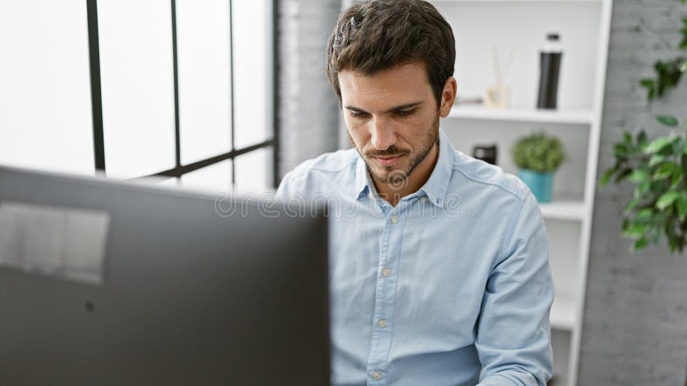A Focused Young Hispanic Man with a Beard Working on a Computer in a ...
