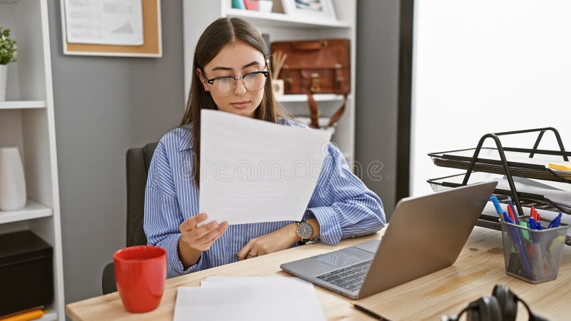 Focused Young Hispanic Woman Reviewing a Document in an Office Setting ...