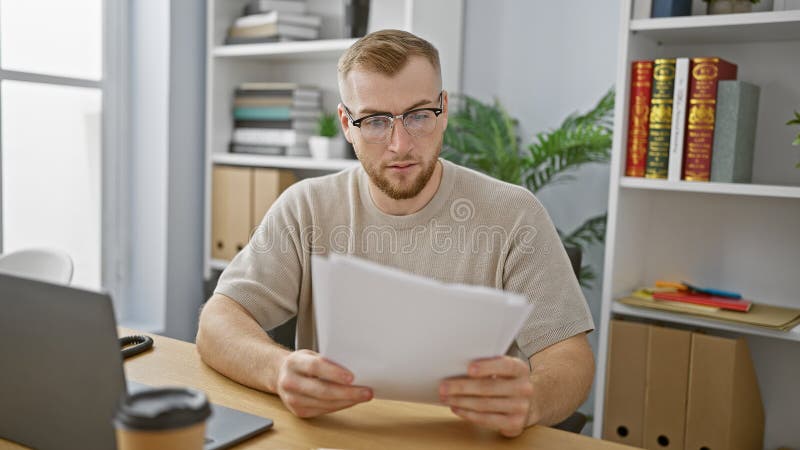 Focused Young Man with Beard Reading Documents in Modern Office Stock ...