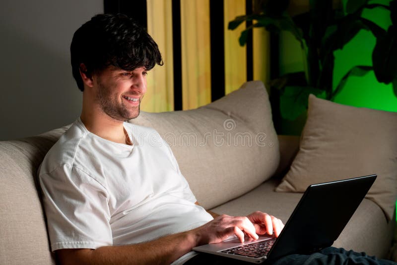 Focused Young Man is Sitting at Home with a Laptop on the Couch. Man ...