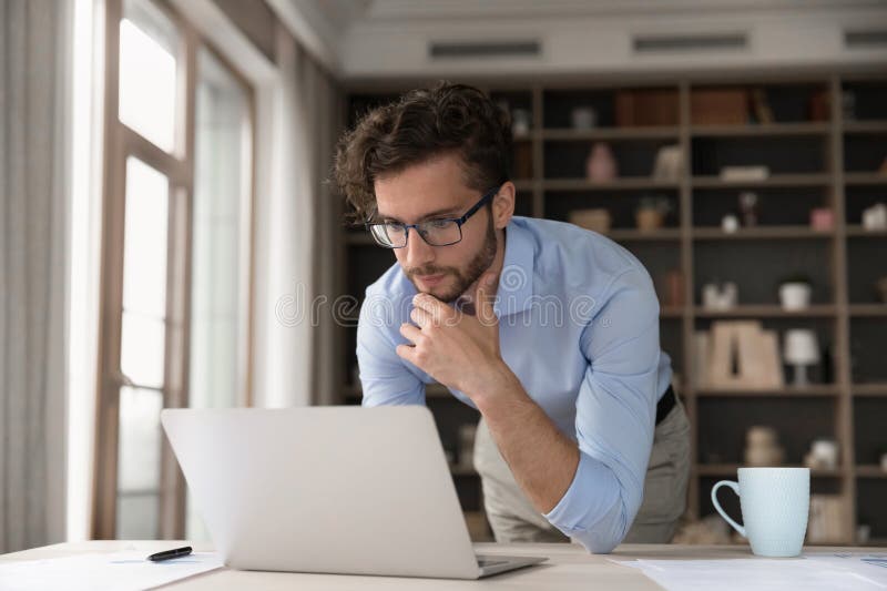 Focused Young Man Stand at Workplace Lean Forward To Notebook Stock ...