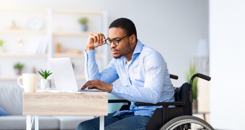 Focused Young Man in Wheelchair Using Laptop Computer for Online Work or Communication at Home ...