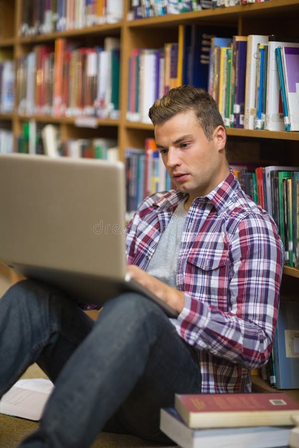 Focused Young Student Sitting on Library Floor Using Laptop Stock Photo ...