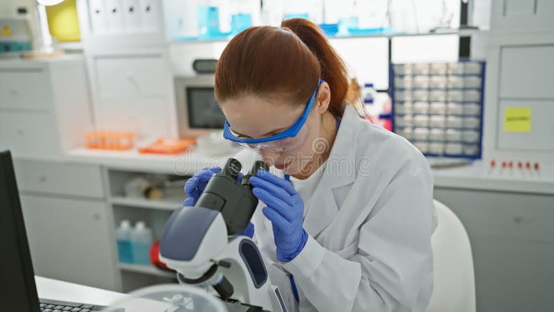 A Focused Young Woman in a Lab Coat Examines Samples Under a Microscope ...