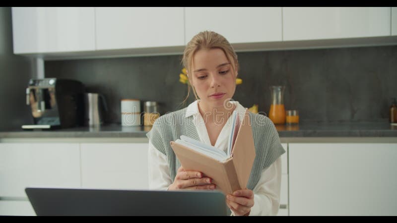 Focused Young Woman Reading a Book while Working Remotely from Her ...