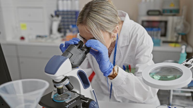 A Focused Young Woman Scientist Examines a Sample through a Microscope ...