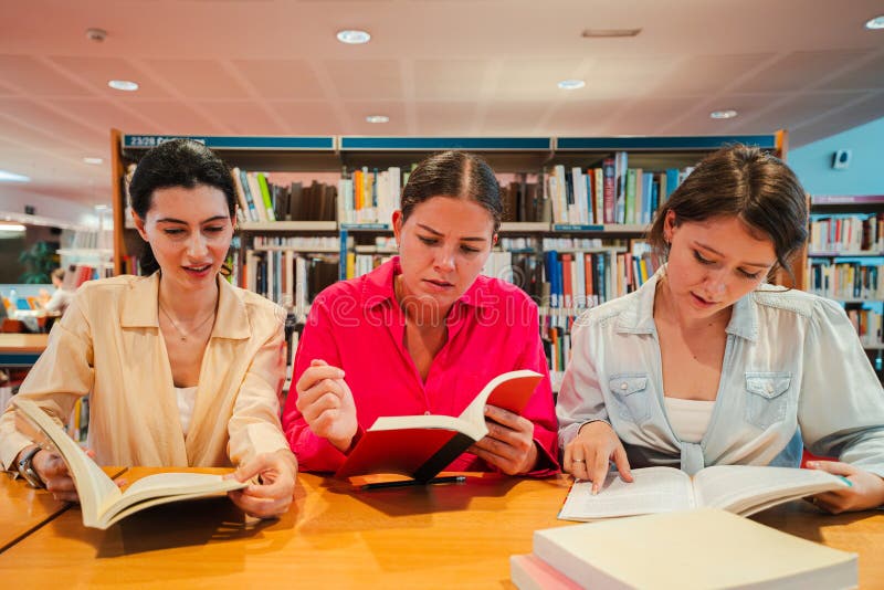 Focused Young Women Engaged in Intense Reading Session with Books in a ...
