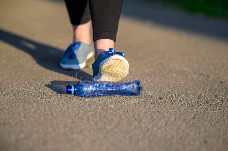 A Foot in a Boot Presses an Empty Plastic Bottle on an Asphalt Pavement ...