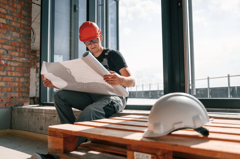 Foreman in Hard Hat is Sitting Indoors and Reading Plan of the Building ...