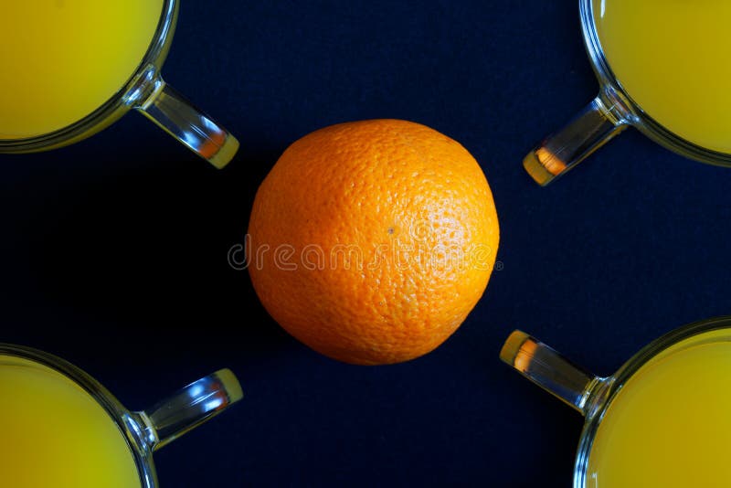 Four Clear Orange Juice Mugs and One Fresh Orange on a Dark Surface ...