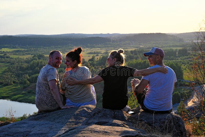 Four Friends Sitting on Edge of Mountain at Sunset Stock Photo - Image ...