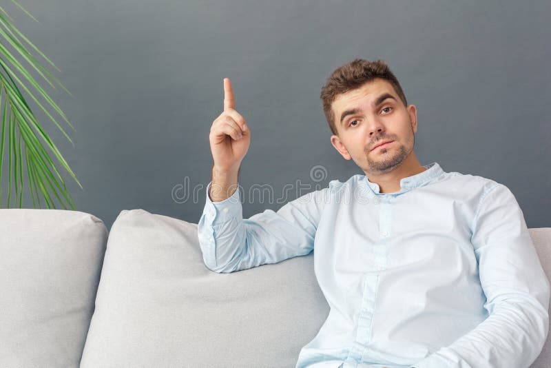 Freestyle. Young Man Studio Sitting on Sofa on Grey Pointing Up ...